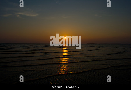 sun setting above the water with reflections in water Stock Photo - Alamy