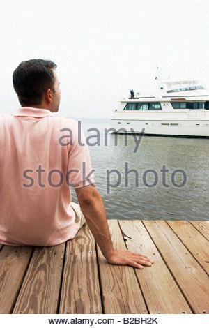 People sitting on a dock watching the sailboats in the Charles River ...