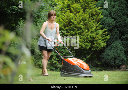 Lady cutting grass with red Flymo mower approaching yellow Dandelion ...