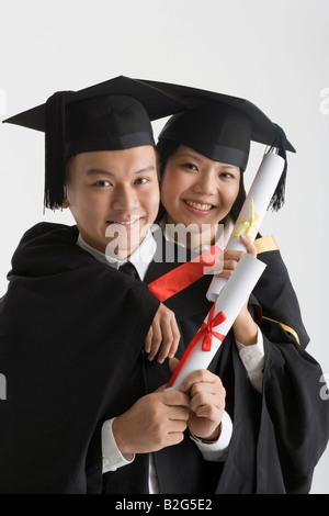Two excited asian graduate students carrying certificate on white ...
