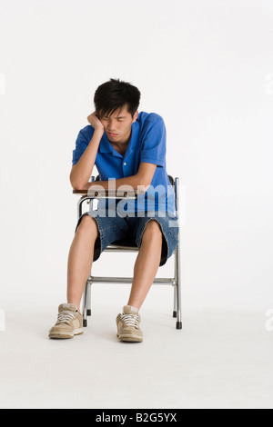 Young man napping on a writing chair Stock Photo - Alamy