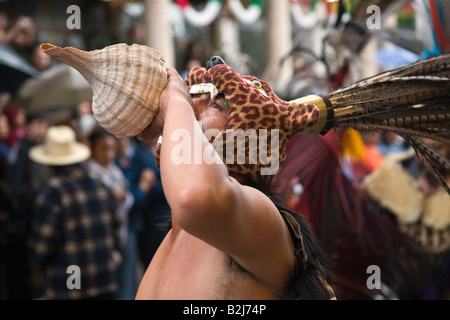 An AZTEC DANCER blows a CONCH in a traditional feathered warrior ...