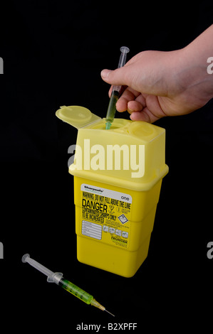 disposing of a hypodermic syringe and needle in a yellow plastic sharps ...