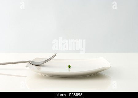 One single pea on a plate, hand with tape measure and fork, diet and ...