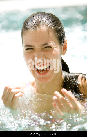 A pretty young woman relaxes by the water, holding a drink while ...