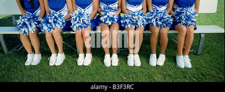 Group of cheerleaders sitting in row on bench, low section Stock Photo ...
