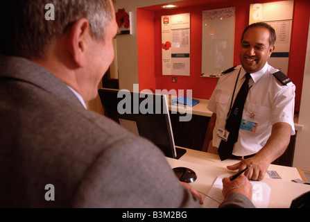 A GUEST SIGNS IN HELPED BY A SECURITY GUARD AT A HOTEL RECEPTION DESK ...