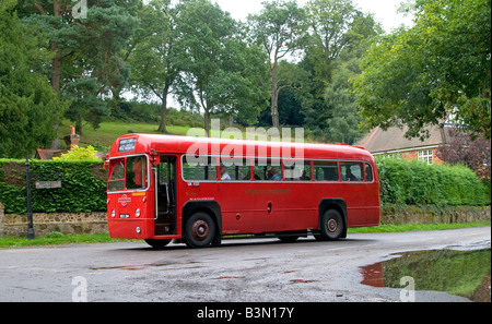 Old fashioned red English bus driving through the countryside in Surrey ...