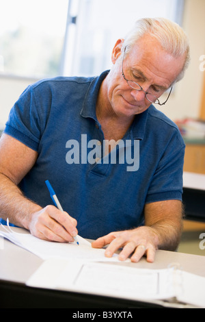 Senior man taking notes while learning online at table indoors. Self ...