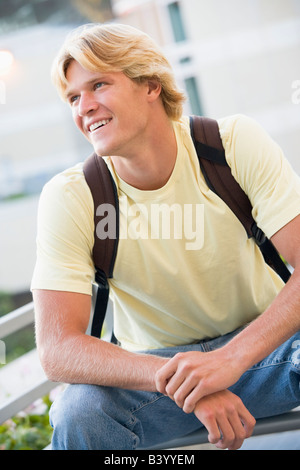 Portrait of happy young student sitting outdoors on steps with laptop ...
