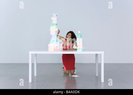 Woman kneeling beside table, looking at stack of boxes Stock Photo - Alamy