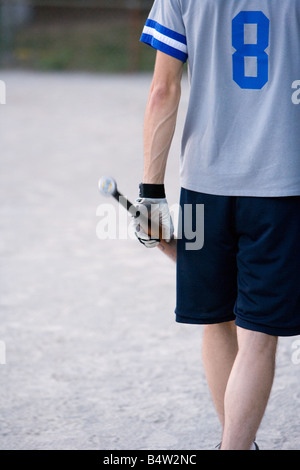 Young man carrying a bat walking towards the baseball field at a park ...