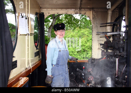 A train engineer in blue overalls crouching down and applying motor oil ...