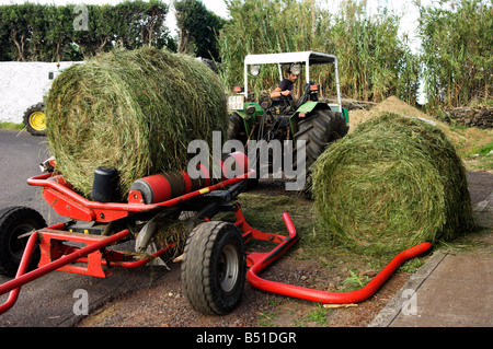 Tractor picking up round hay bail with autowrap machine Stock Photo - Alamy