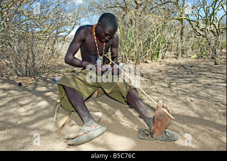 A member of the Hadza tribe shapes a hunting arrow with a knife Lake ...