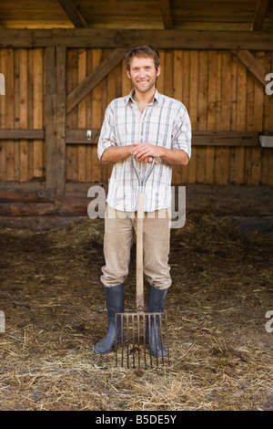 full length view of farmer with hayfork standing near cowshed on dairy ...