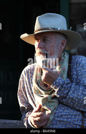 An old timer cowboy leaning against the chuck wagon taking a drink ...