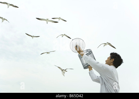 Man releasing bird outdoors, open cage in hand Stock Photo - Alamy