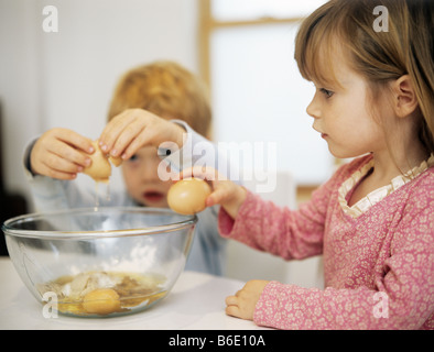Making cakes. Two three year old children mixing eggs, sugar and flour ...