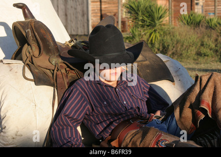 A young cowboy resting against his bed roll and saddle out on the range ...