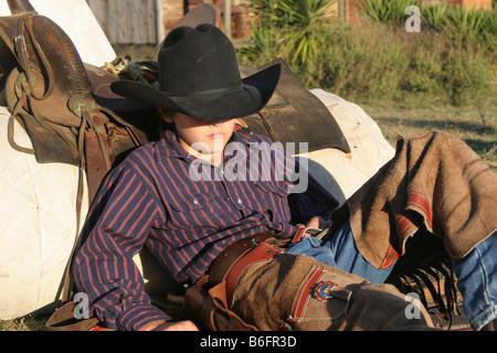 A young cowboy resting against his bed roll and saddle out on the range ...