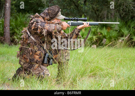 Hunter wearing camouflage outfit with hunting bow kneels in the woods ...