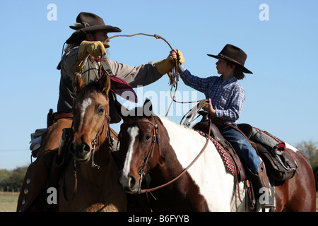 A cowboy father on horseback showing his son how to throw a rope to ...