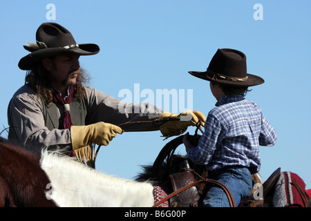 A cowboy father showing his son how to rope a cow on the ranch by ...