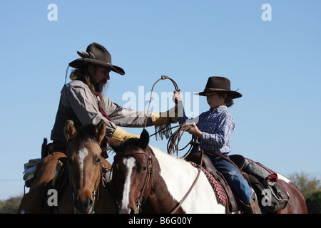 A cowboy father on horseback showing his son how to throw a rope to ...