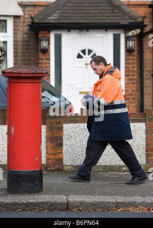 A Royal Mail postman walks along a road to deliver letters through a ...