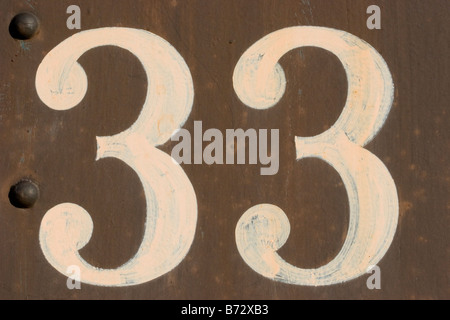 Number 33, thirty-three, old house number plate on a weathered wall ...