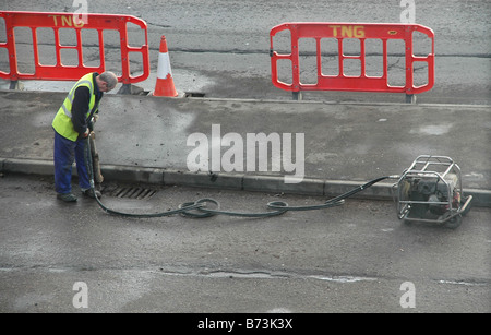 Roadworks Workman uses a pneumatic drill to dig a hole in the road ...