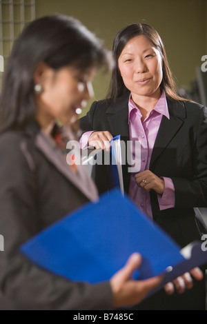 Two Asian businesswomen talking by lectern in boardroom Stock Photo - Alamy