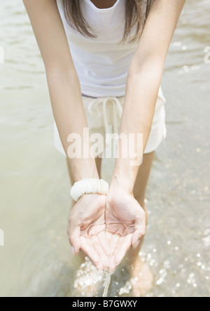 Hand scooping up water in a glass into a still lake at sunrise in India ...
