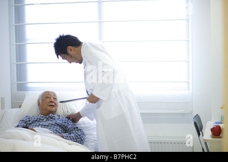 On their ward rounds, two doctors in hospital bedside consultation with ...