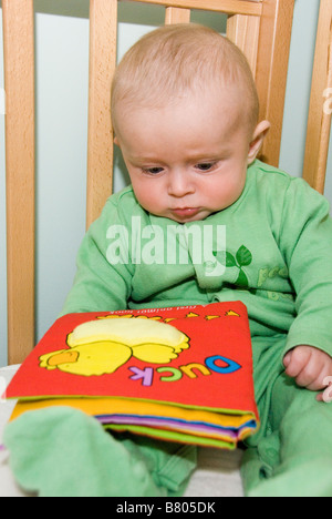 Boy reading open book at white table in school library reading corner ...