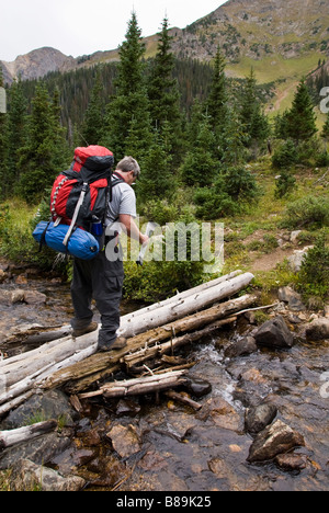 Backpacker crossing a log over a stream in Oregon's Wallowa Mountains ...