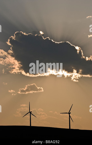 Two wind turbines stand silhouetted against a vibrant orange sunset sky ...