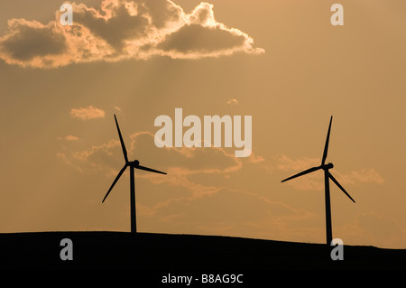 Two wind turbines stand silhouetted against a vibrant orange sunset sky ...