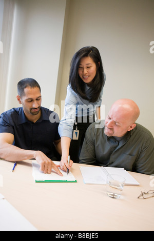 Three colleagues discuss documents while sitting on a couch in an ...
