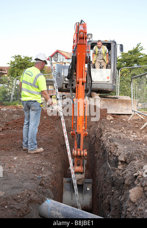 workman measures the depth of a trench dug by a jcb Stock Photo - Alamy