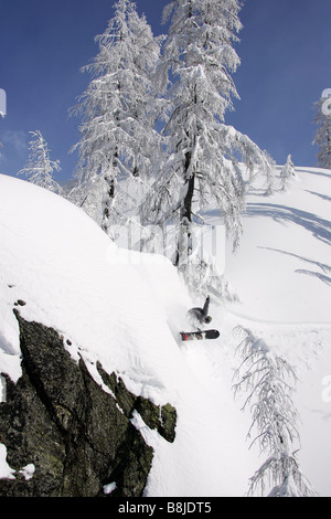 Snowboarder jumping off a cliff off piste, backlit by the sun on a ...
