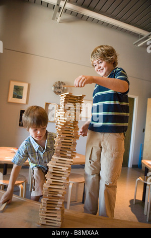 two boys enjoying themselves, building a tall tower out of wood blocks ...