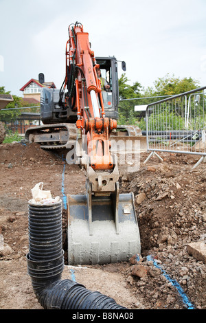 Jcb digging a trench on a construction site while a workman measures ...