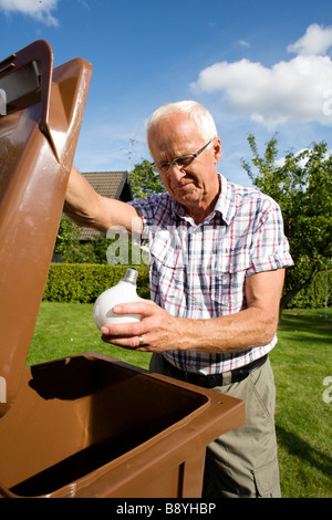 Elderly man with a recycling bin throwing a garbage bag in a trash can ...