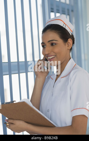 Nurse smiling while talking on a mobile phone inside a car before or ...