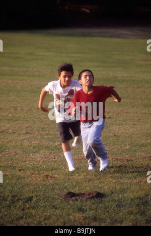Two Hispanic boy chase tag run play park grass enjoy fun exercise sport ...