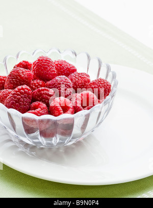 Clear glass bowl of ripe raspberries on a rustic farm picnic table in ...