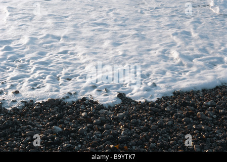 A close up as the foamy sea surf washes up over a people beach on the ...