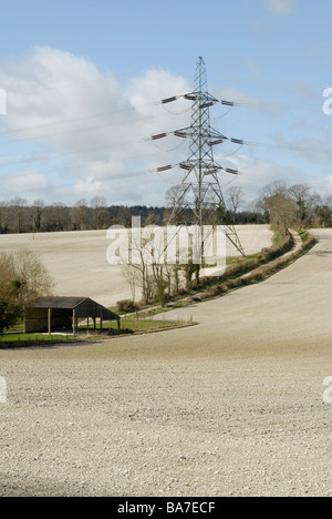 Electricity pylon and cables casting shadows across chalky fields of ...